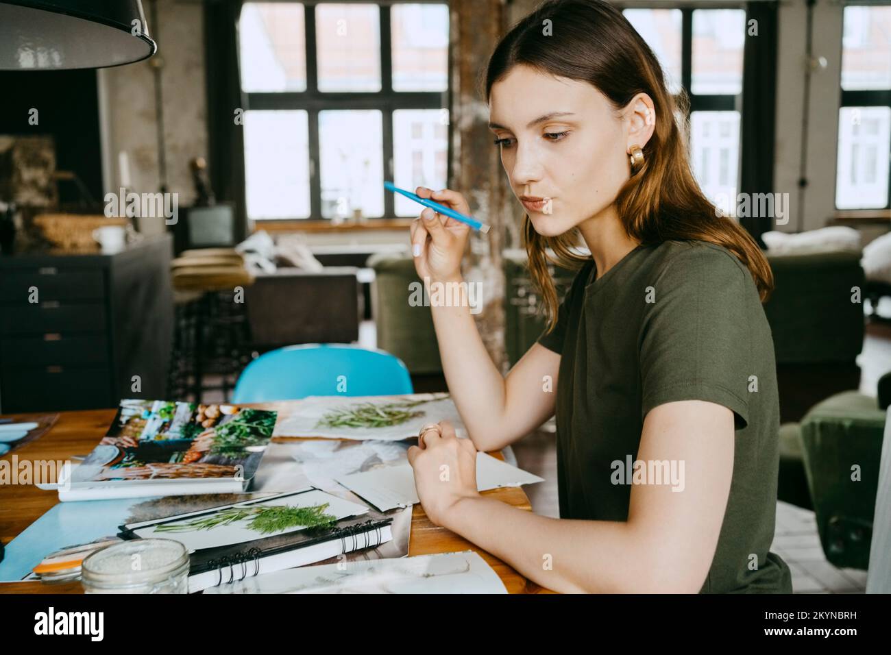 Thoughtful female food stylist puckering lips and holding pen while ...