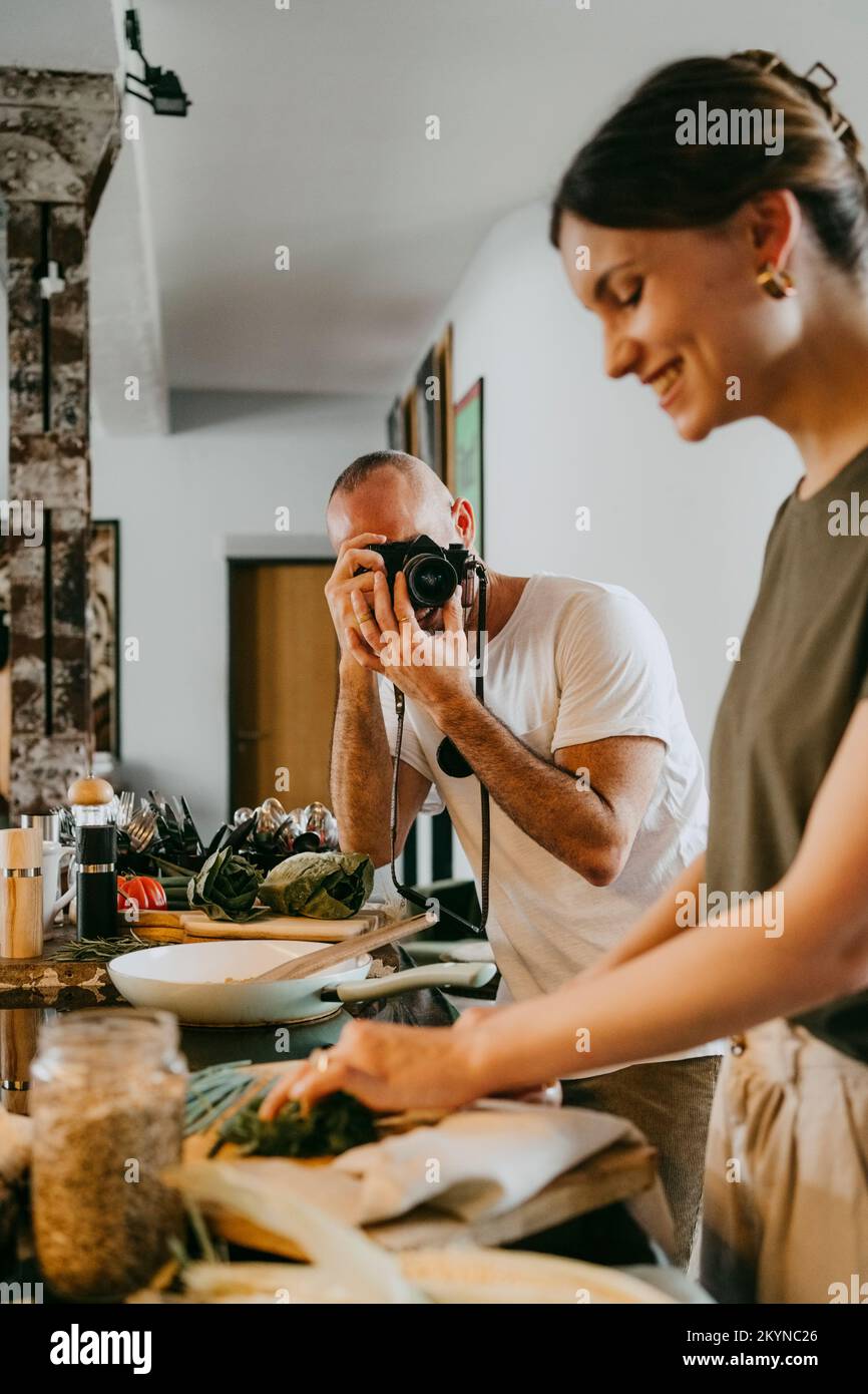 Colleague photographing female chef through camera while preparing food ...