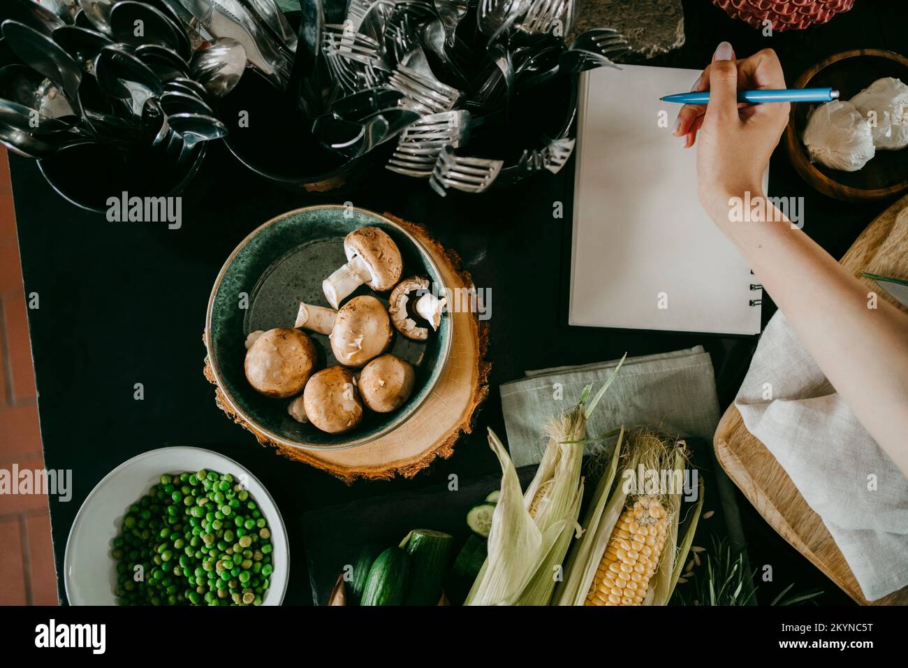 Hand of female chef writing recipe in diary by vegetables and cutlery ...