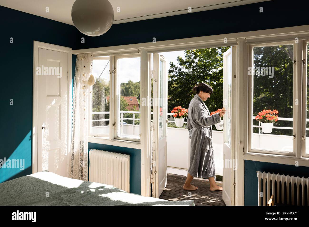 Side view of smiling woman wearing bathrobe while opening balcony door ...