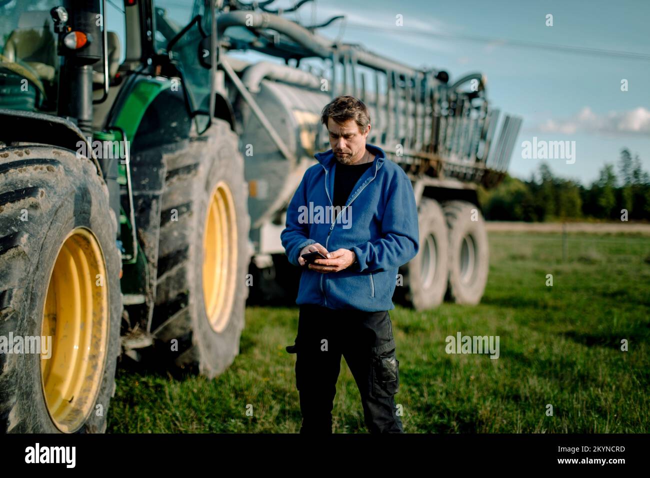 Mature farmer using smart phone standing against tractor on field Stock ...