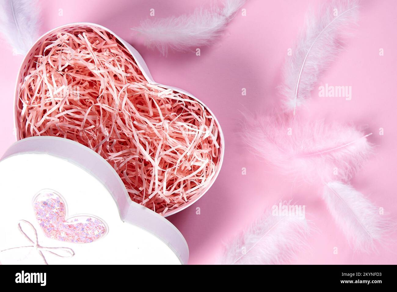 Heart-shaped gift box on a pink background with feathers . Layout for ...