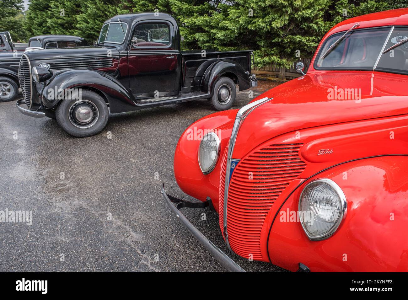 Partial view of a old bight red restored Ford car parked by a black ...