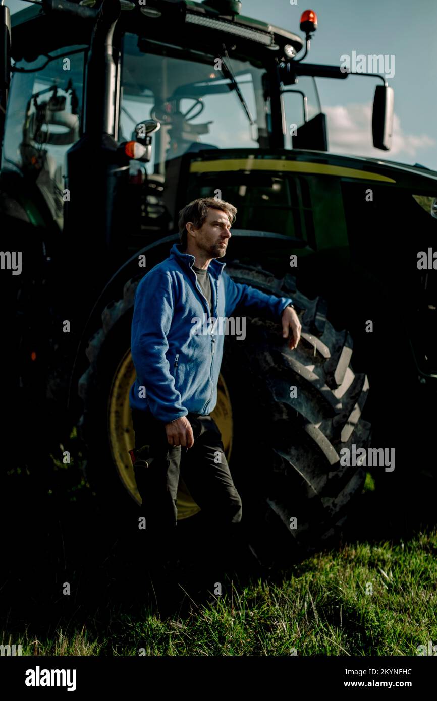 Contemplative farmer standing by tractor at farm Stock Photo - Alamy
