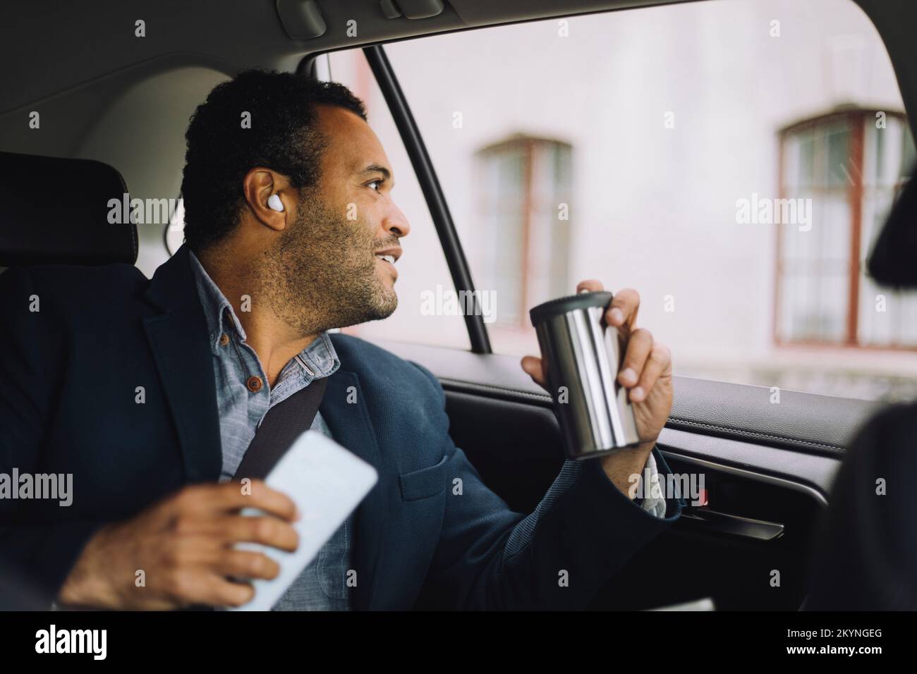 Smiling male commuter with insulated drink container and smart phone ...