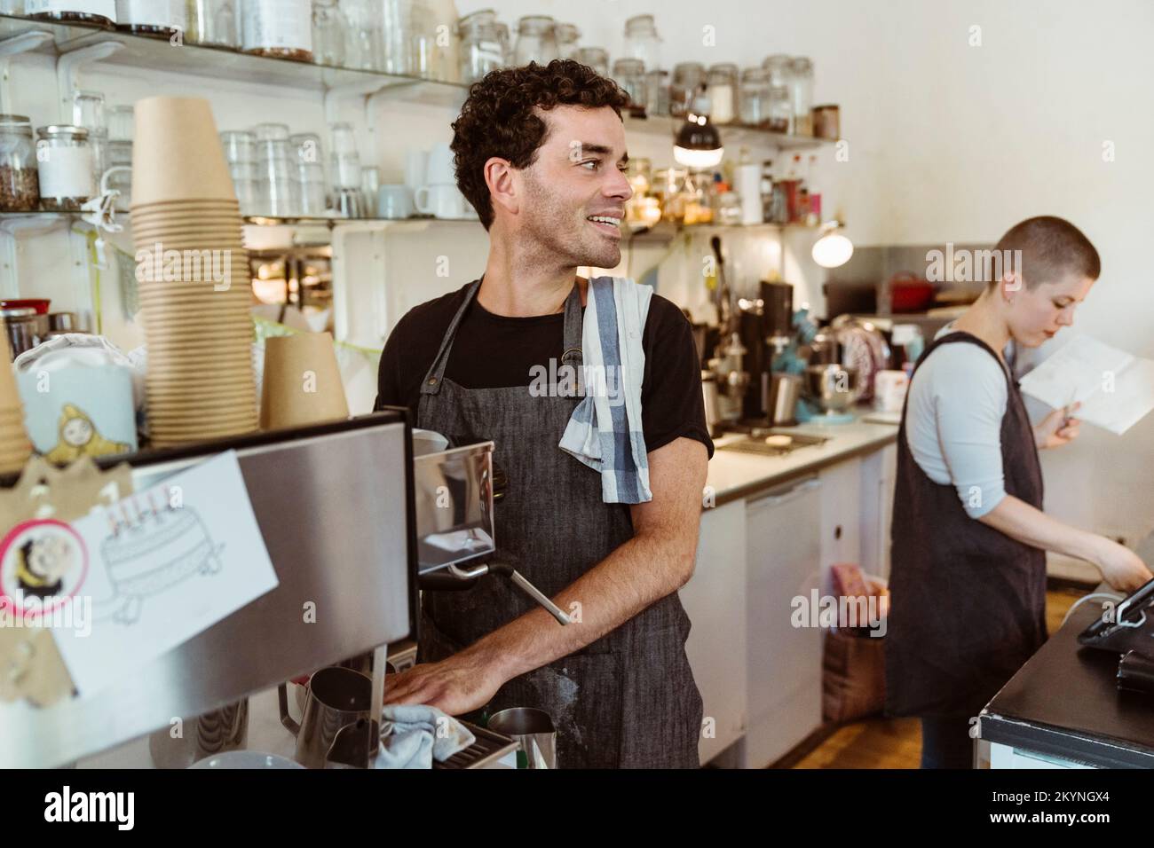 Smiling owner wearing apron looking away while standing near coffee ...