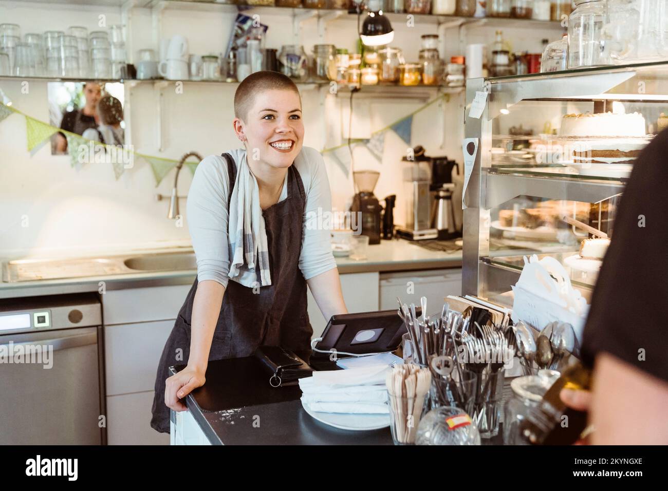 Happy female owner leaning on counter while looking at colleague in ...