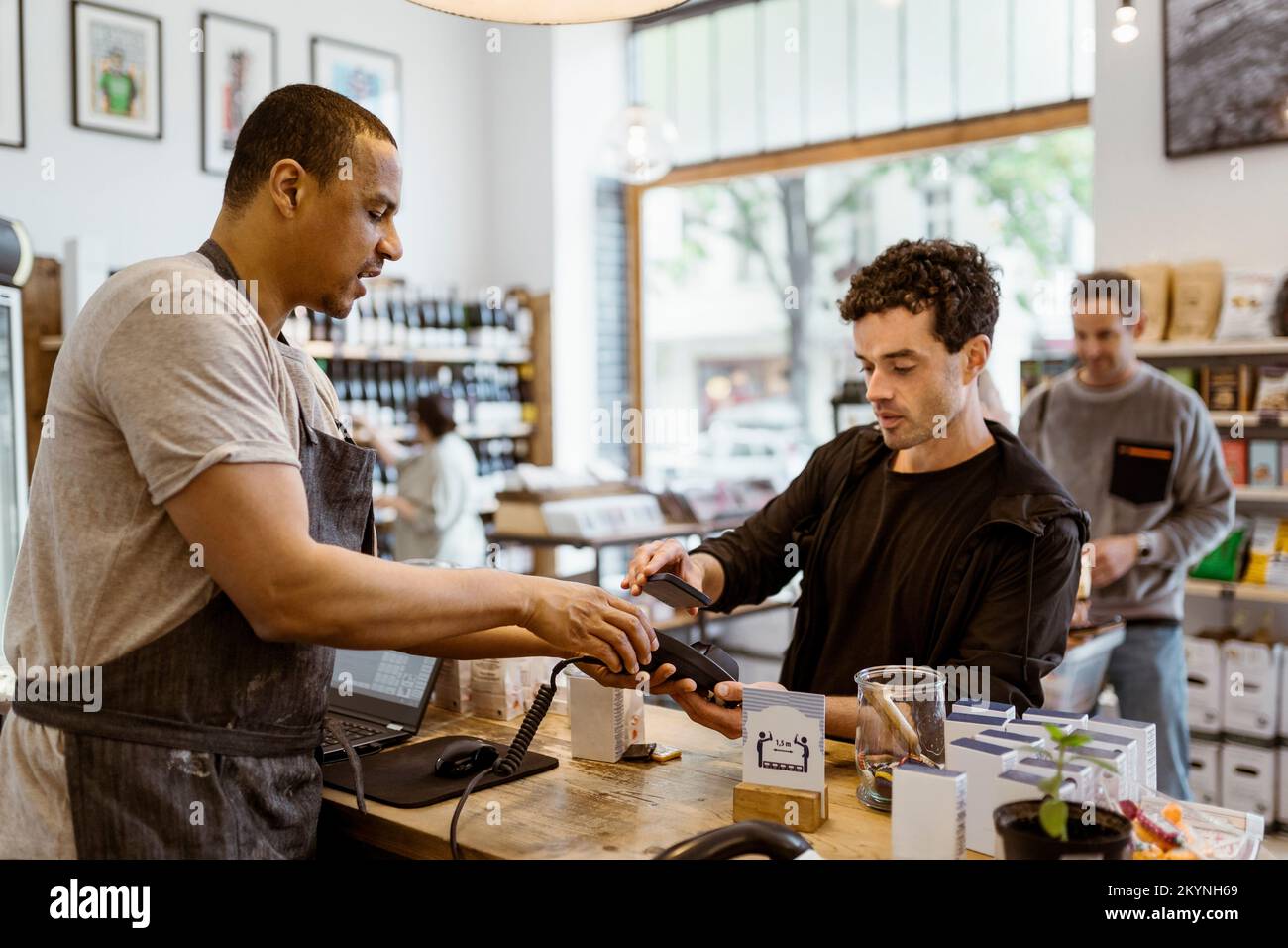 Side view of male owner assisting customer doing online payment at ...