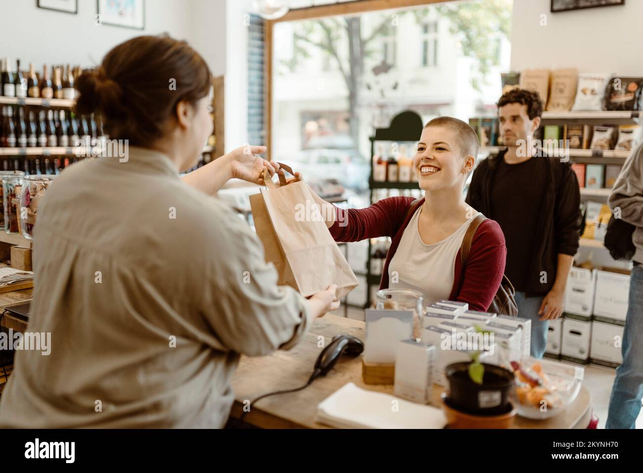Young happy female customer taking paper bag from owner at checkout ...