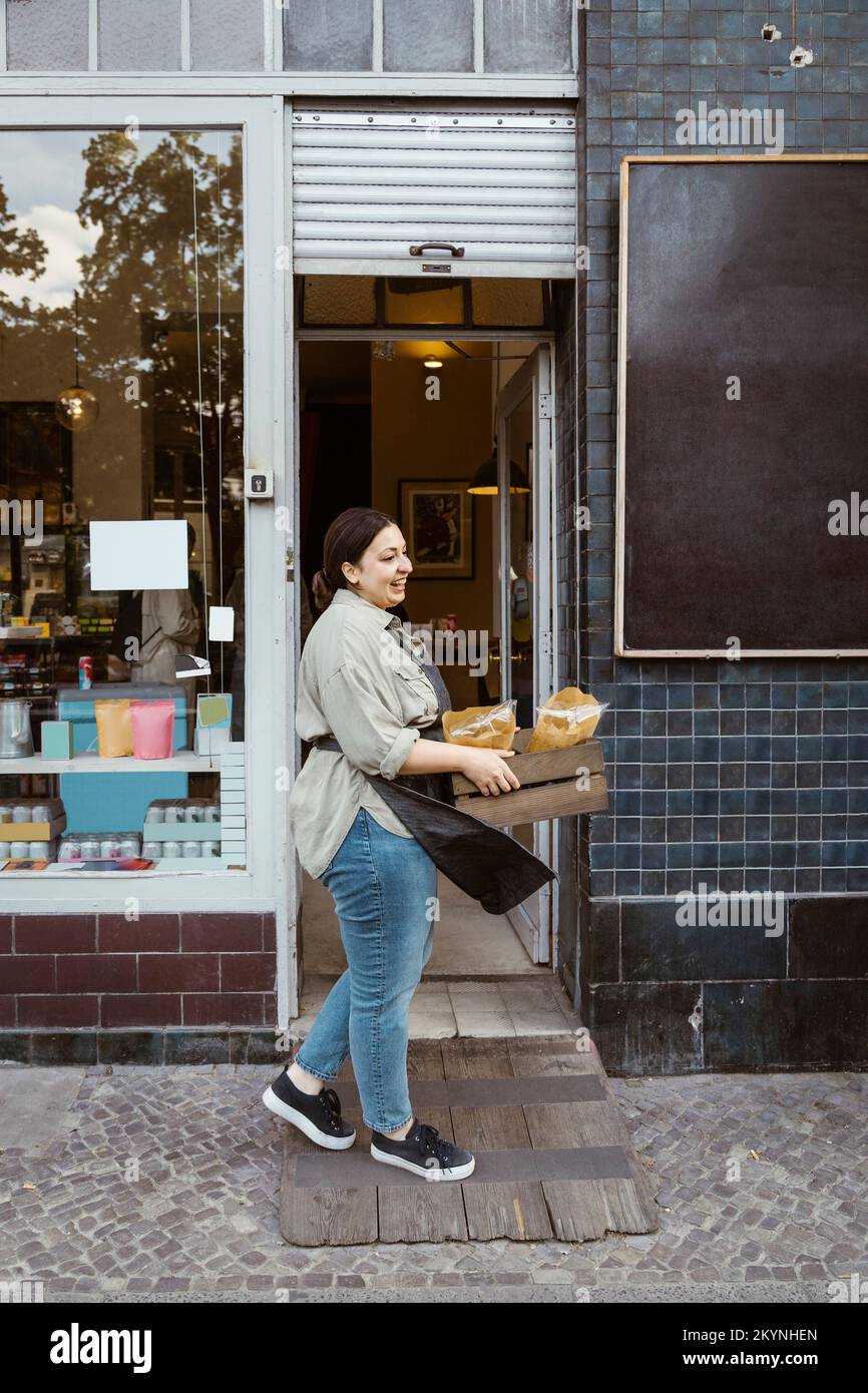 Side view of female owner standing outside deli holding crate Stock ...