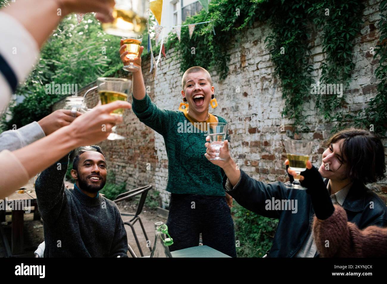 Cheerful woman with mouth open toasting drinks with friends during ...