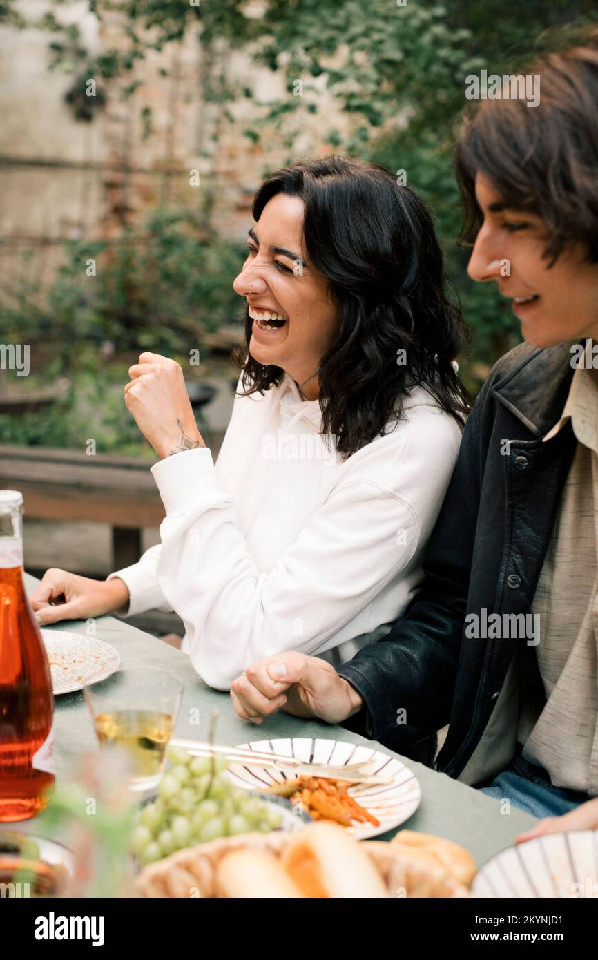 Happy woman laughing while sitting at dining table with male friend ...