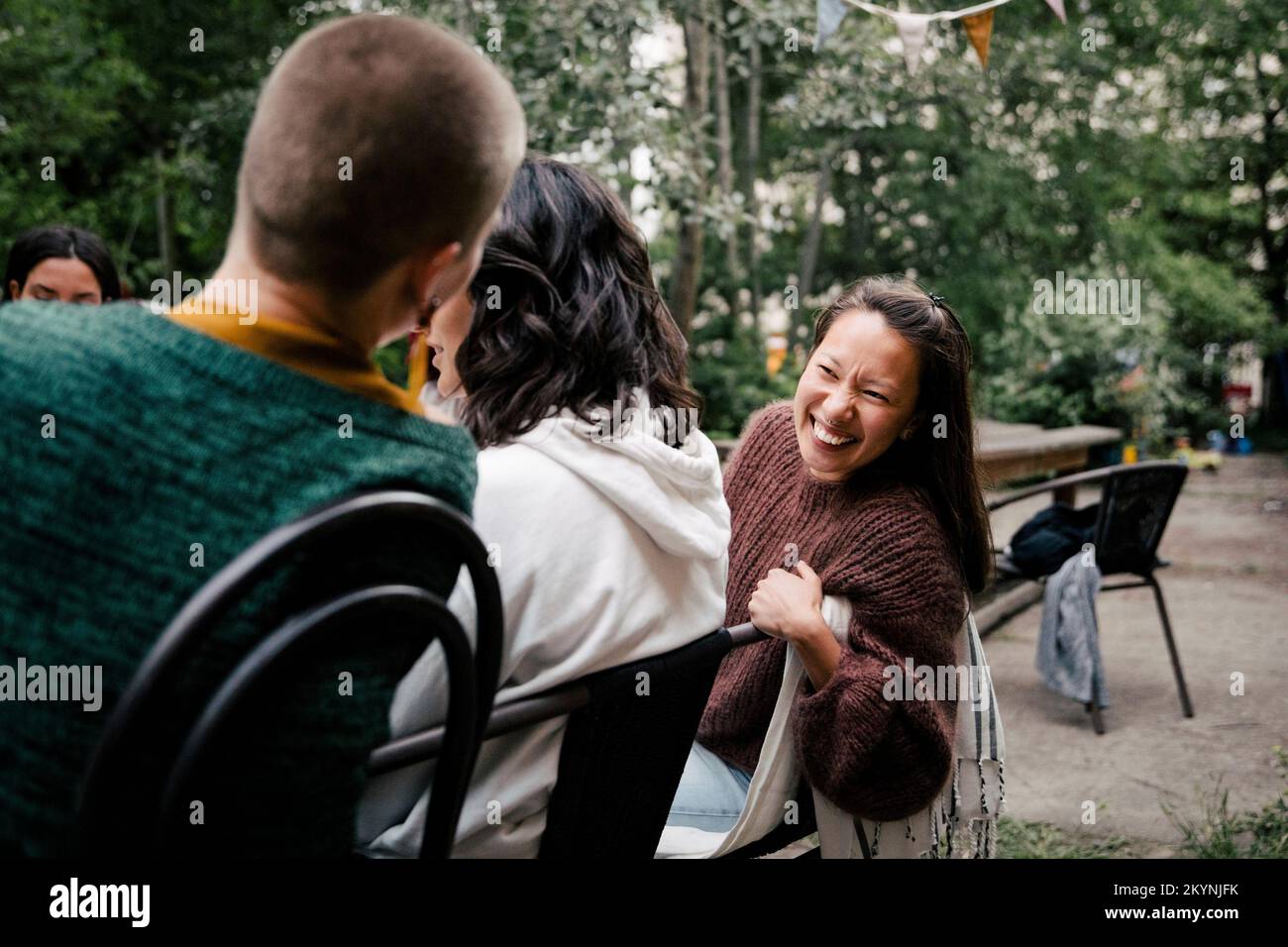 Happy female friends talking to each other sitting on chair at dinner ...