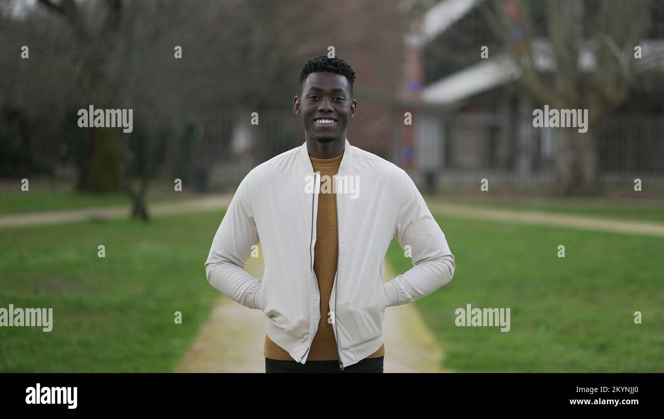 Young friendly black African man standing outside at park smiling at ...