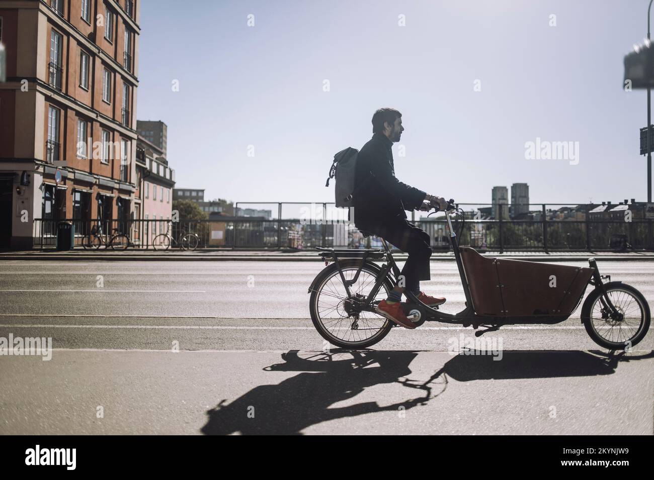 Side view of businessman commuting through cargo bike during sunny day ...
