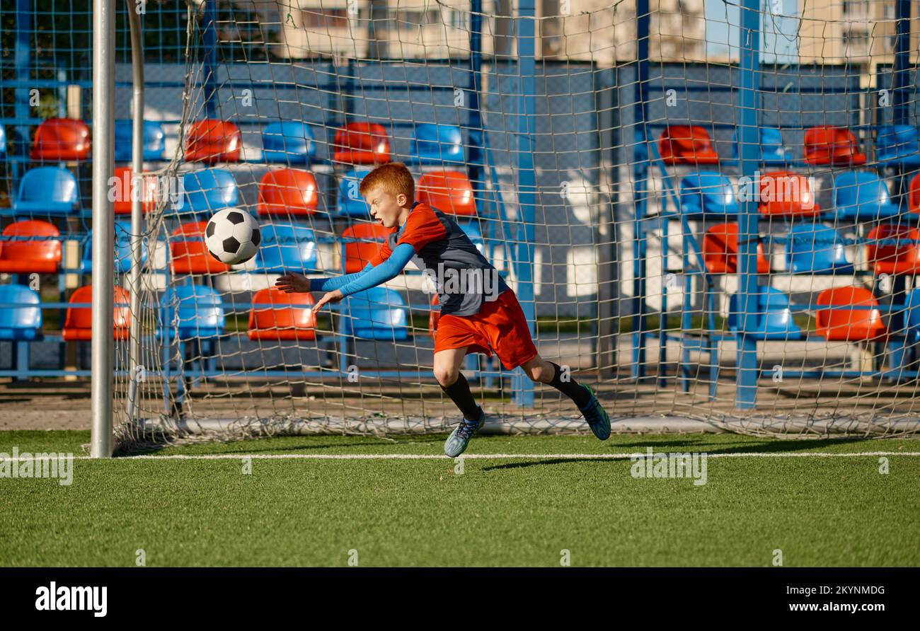 Junior goalkeeper catching ball while defending gate in football match ...