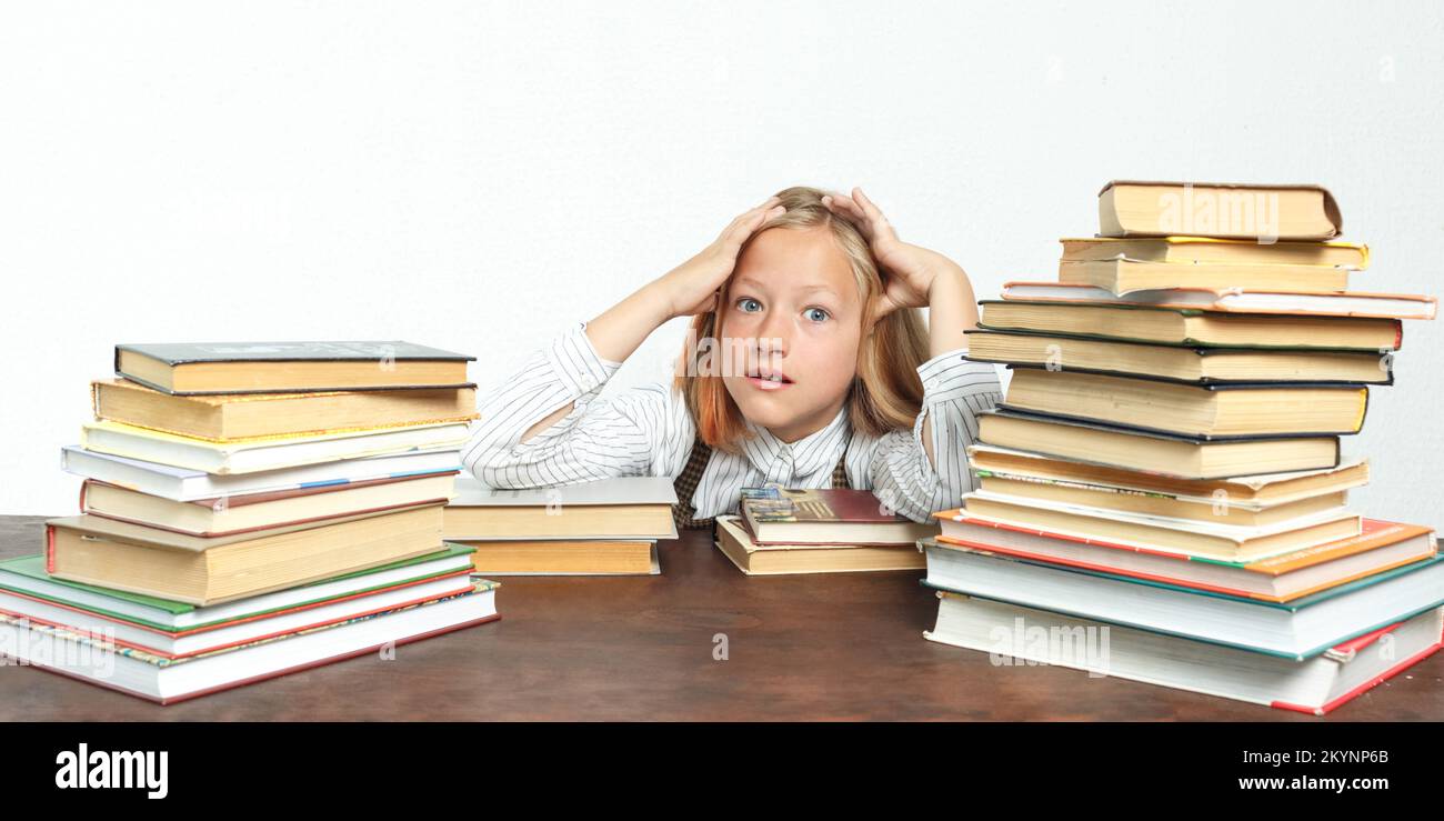 Portrait of a teenage girl sitting at a table tired among the books and ...
