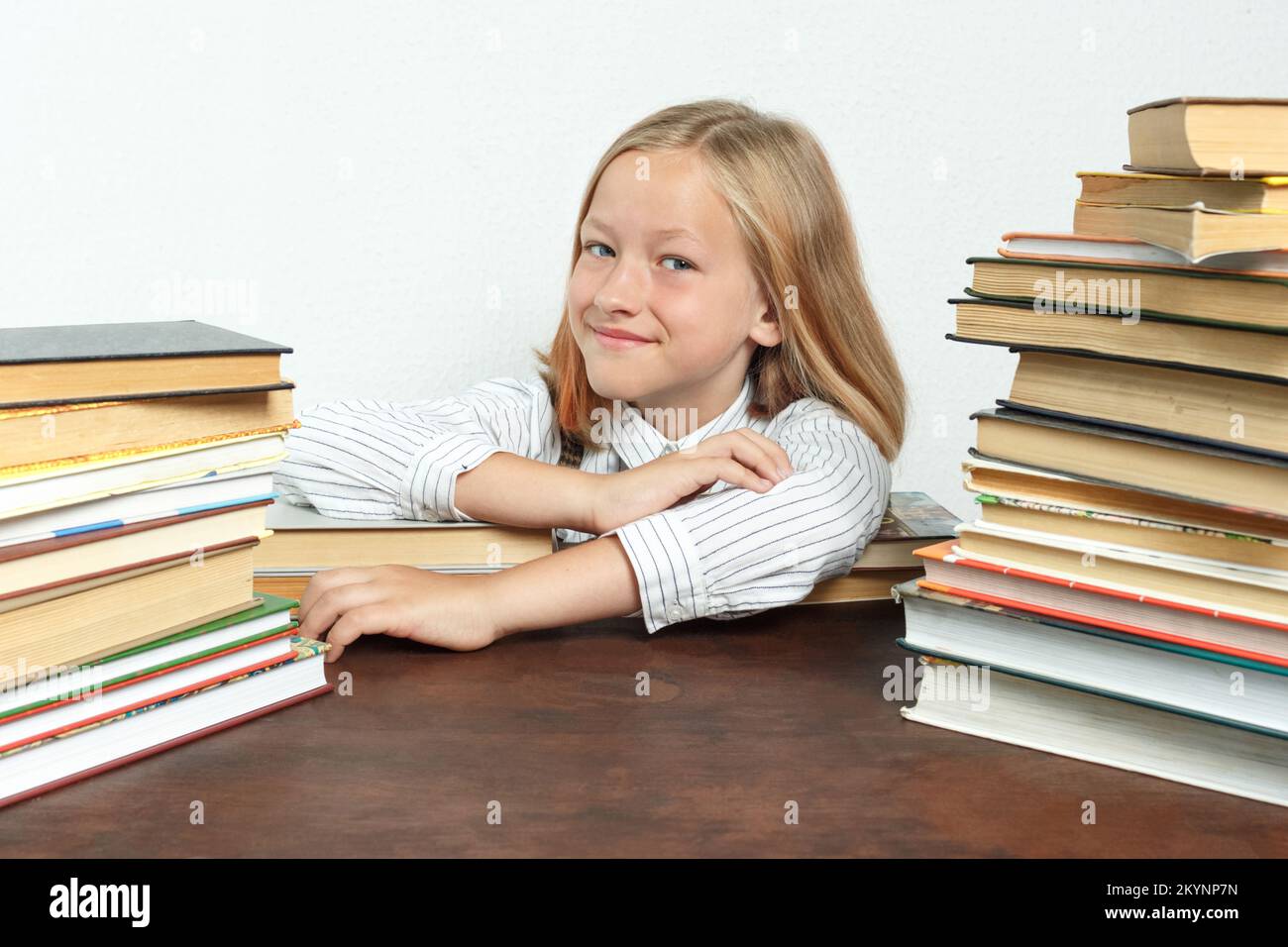 Portrait of a teenage girl who sits at a table among the books. Looks ...