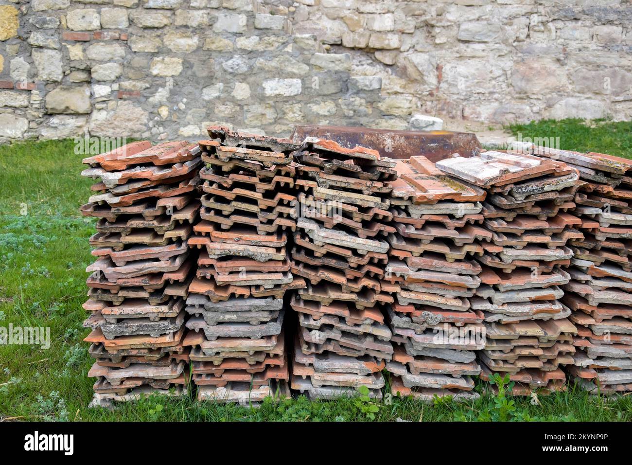 Old clay tiles are stacked on green grass, against background of old ...