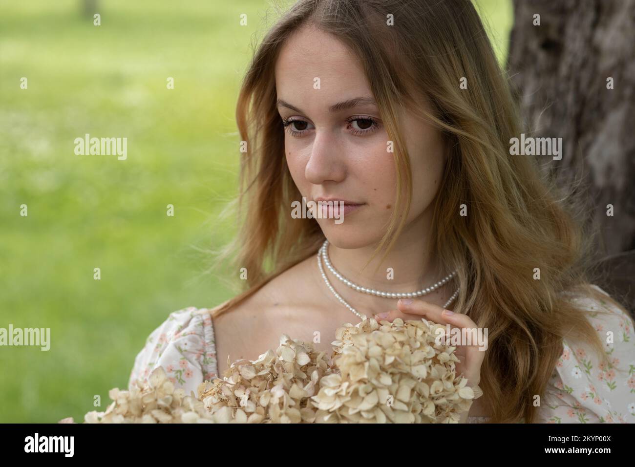 Long-haired young blonde girl with flowers in her hands against the ...