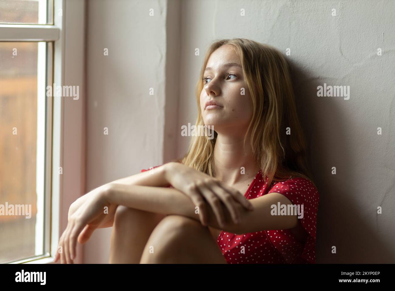 A romantic girl in a red dress sits on the floor near the window and ...