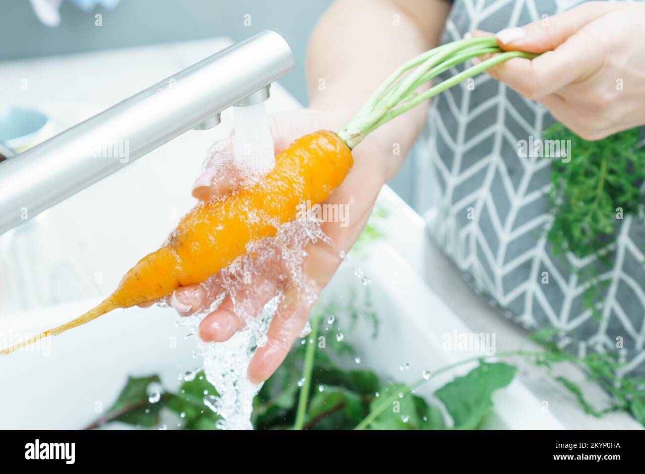 Female hands washing fresh carrot under tap water jet in kitchen sink ...