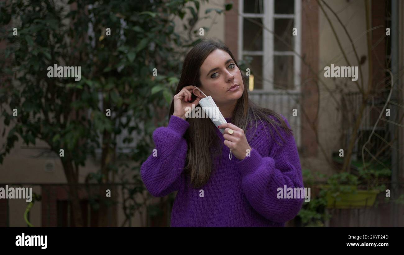Young woman putting covid-19 surgical face mask looking at camera Stock ...