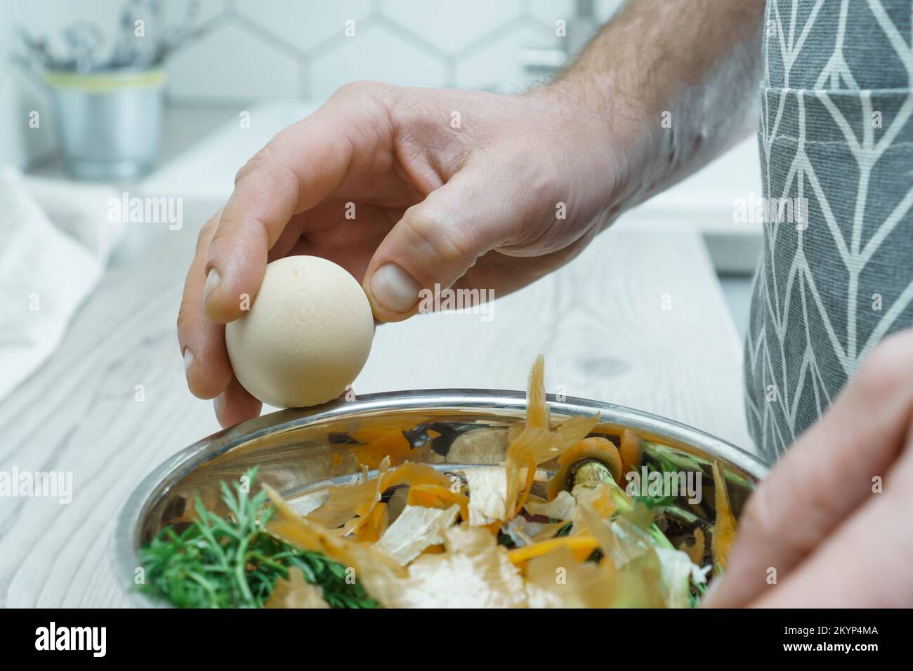 Male hands peeling shell of boiled egg over bowl of vegetable peelings ...