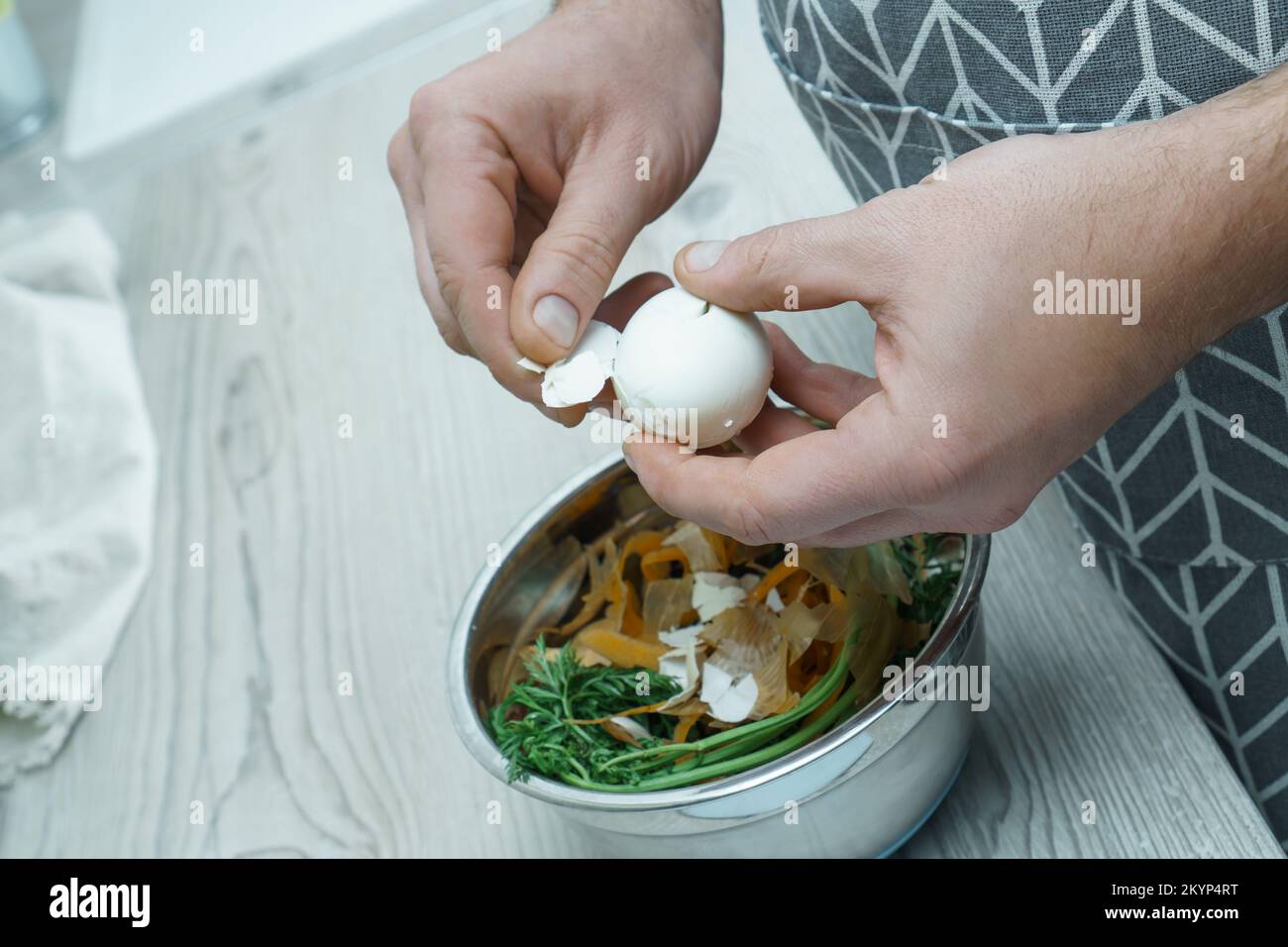 Human hands peeling shell of boiled egg over bowl of vegetable peelings ...