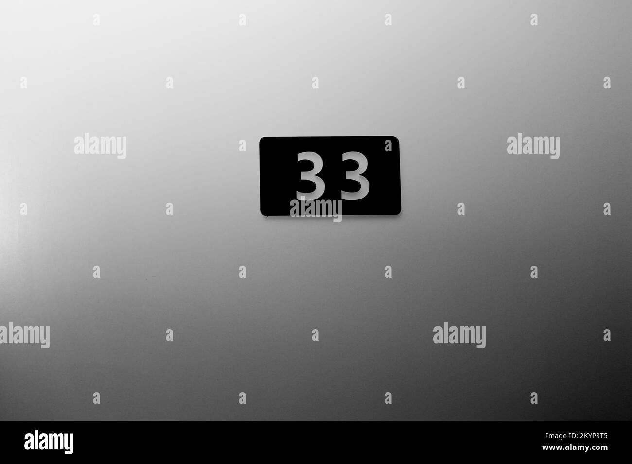 Hotel room 33 number mounted on a white wall. White number on black ...