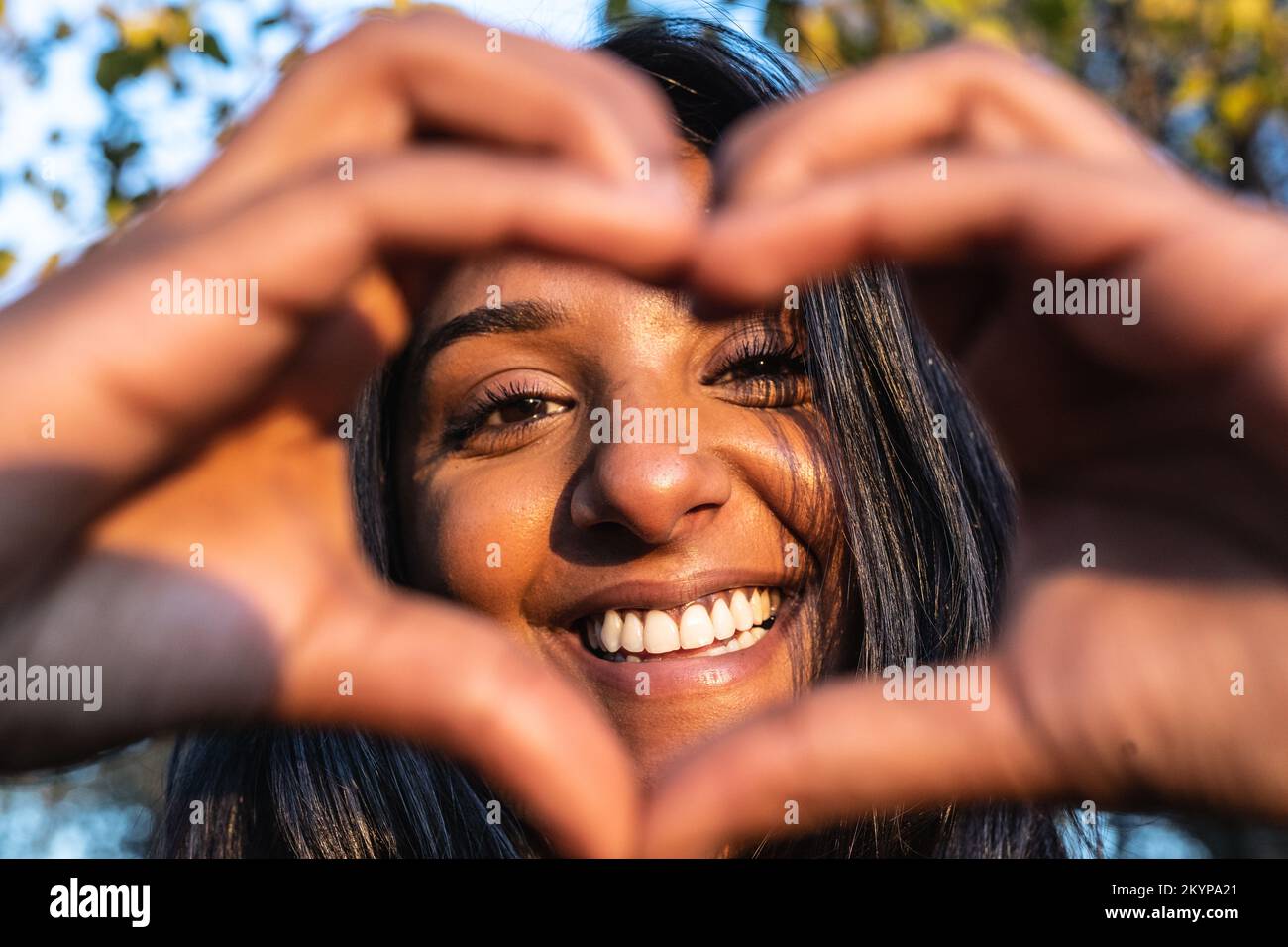Frontal view of happy woman laughing at camera and making a heart shape ...