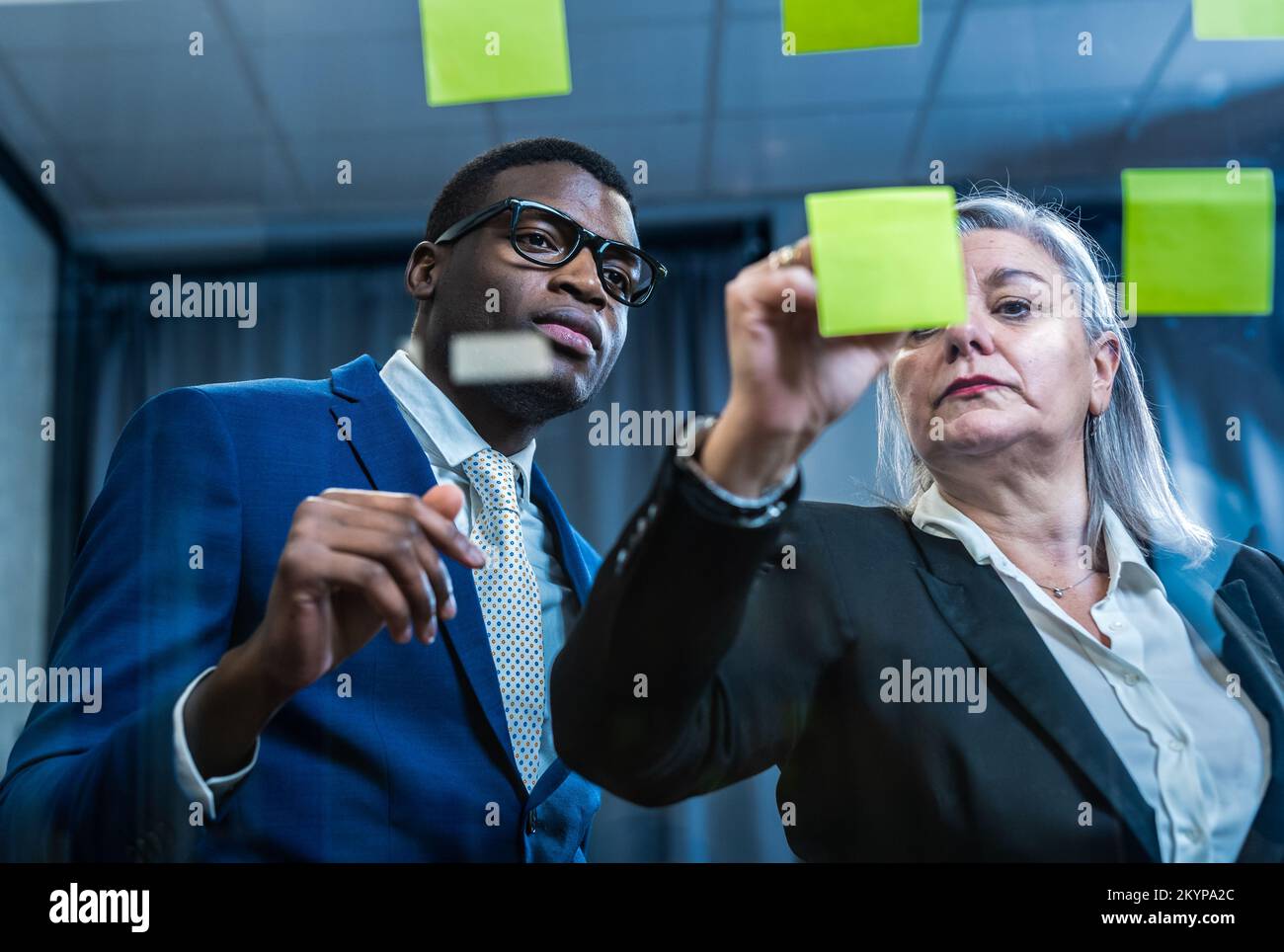 Serious mature businesswoman writing on sticky note in meeting room ...