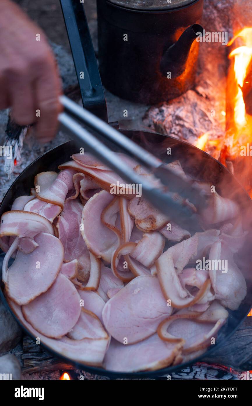 Australian style bacon being cooked over a camfire with silver tongs ...