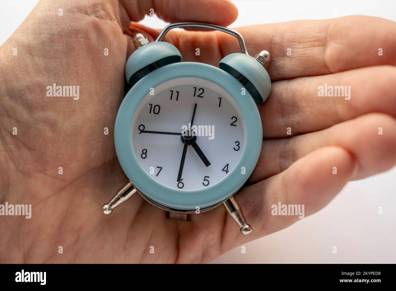 small blue alarm clock in a man's hand. time. the hands of the clock ...