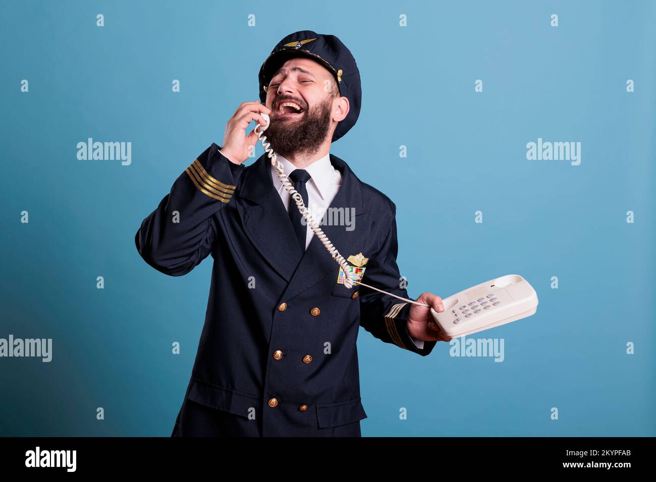 Middle aged airliner captain talking on landline phone, holding ...