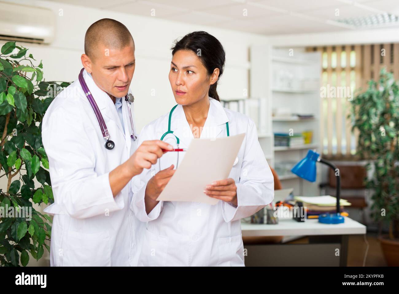 Two doctors discussing medical card of patient in office Stock Photo ...