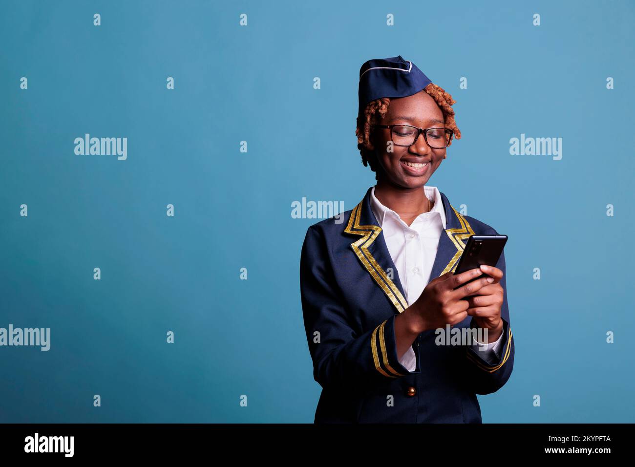 Smiling female flight attendant wearing uniform reading messages on ...