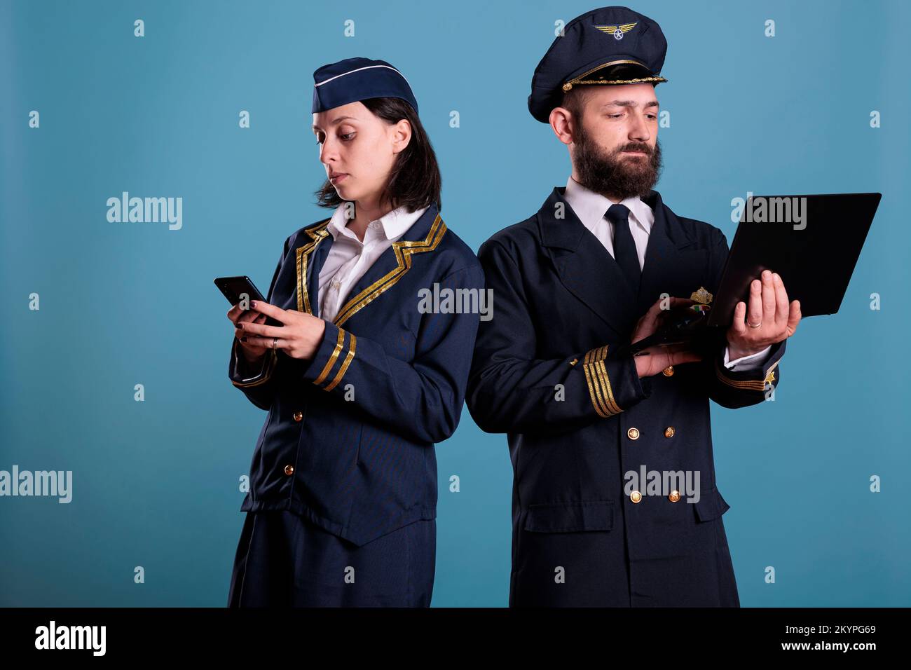 Captain using laptop, stewardess messaging on smartphone. Airlane pilot ...