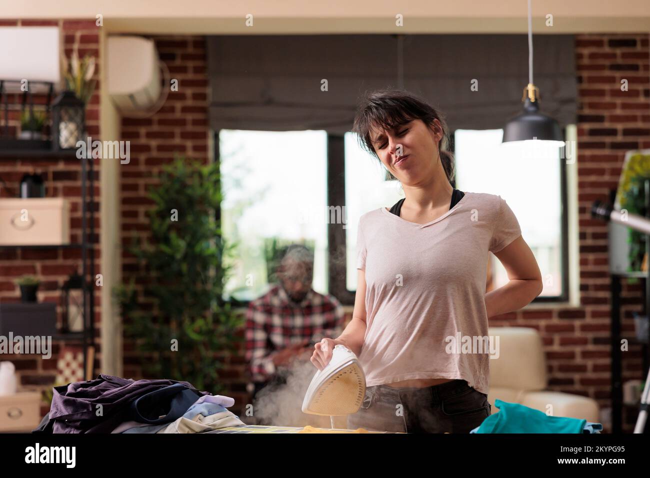 Sore Woman Finishing Housework Using The Steam Iron In The Living Room