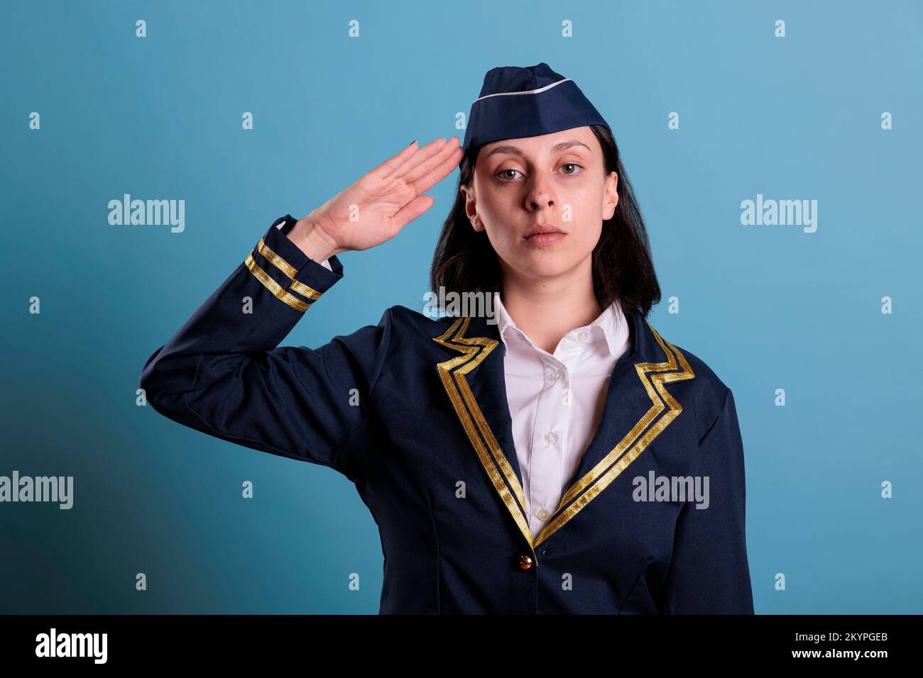 Young serious flight attendant saluting, wearing uniform, standing ...