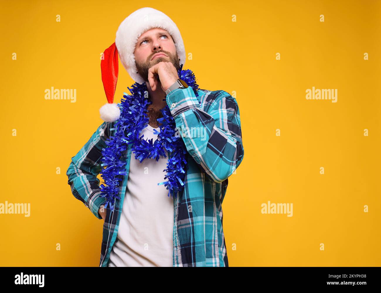 young bearded man in a plaid shirt wearing a santa hat and with a blue ...