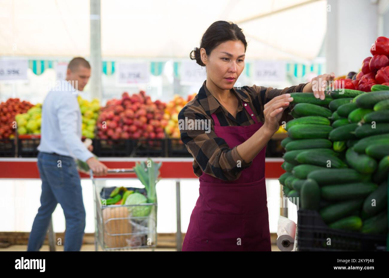 Supermarket worker putting cucumber on counter Stock Photo - Alamy