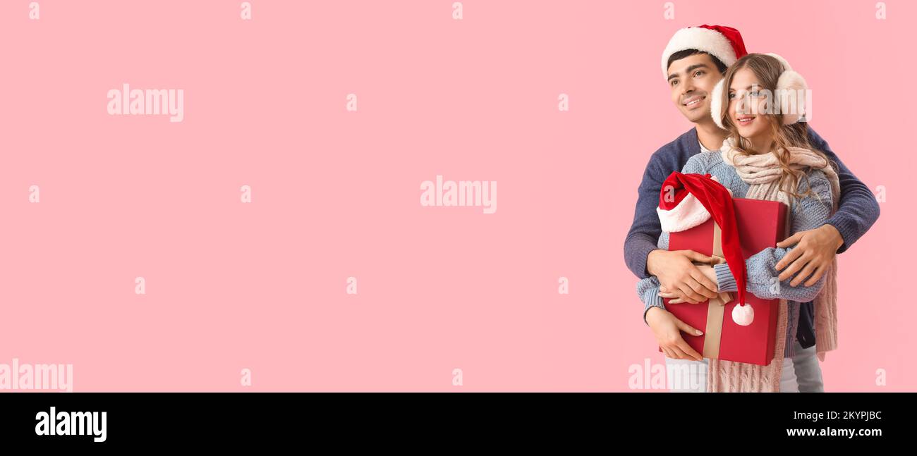 Young couple in love holding Christmas gift on pink background with ...