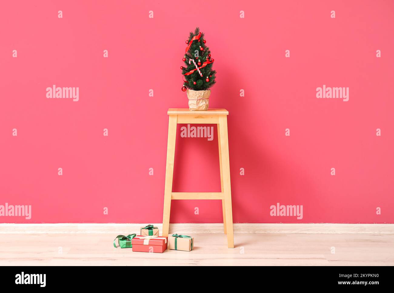 Small Christmas tree on stool and gifts near red wall Stock Photo - Alamy