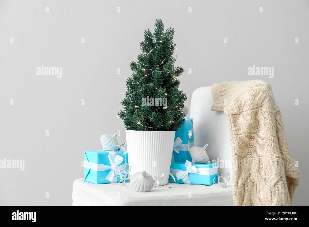 Small Christmas tree with presents on chair near light wall Stock Photo ...