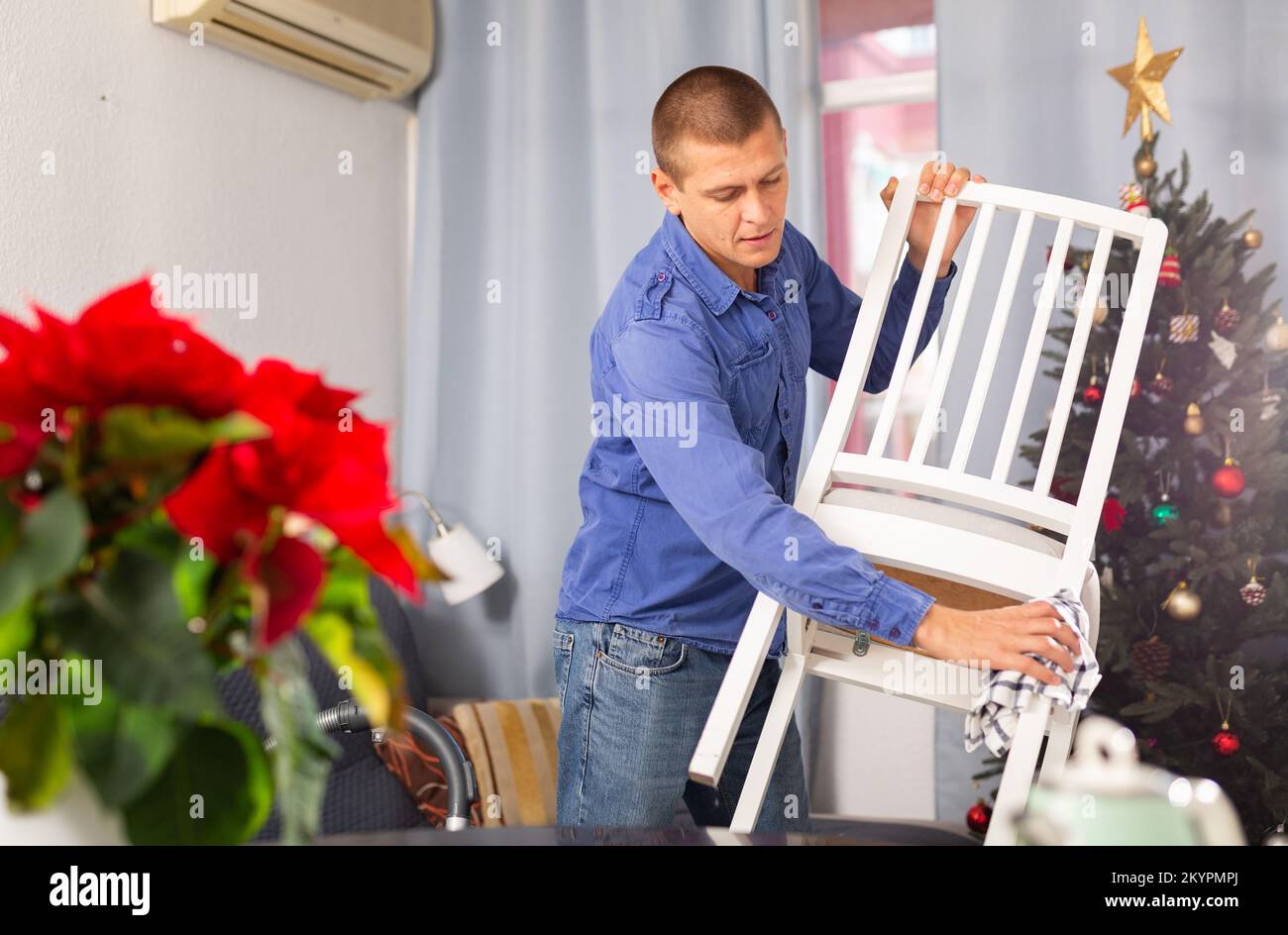 Smiling man wiping dust from a chair in room before christmas Stock ...