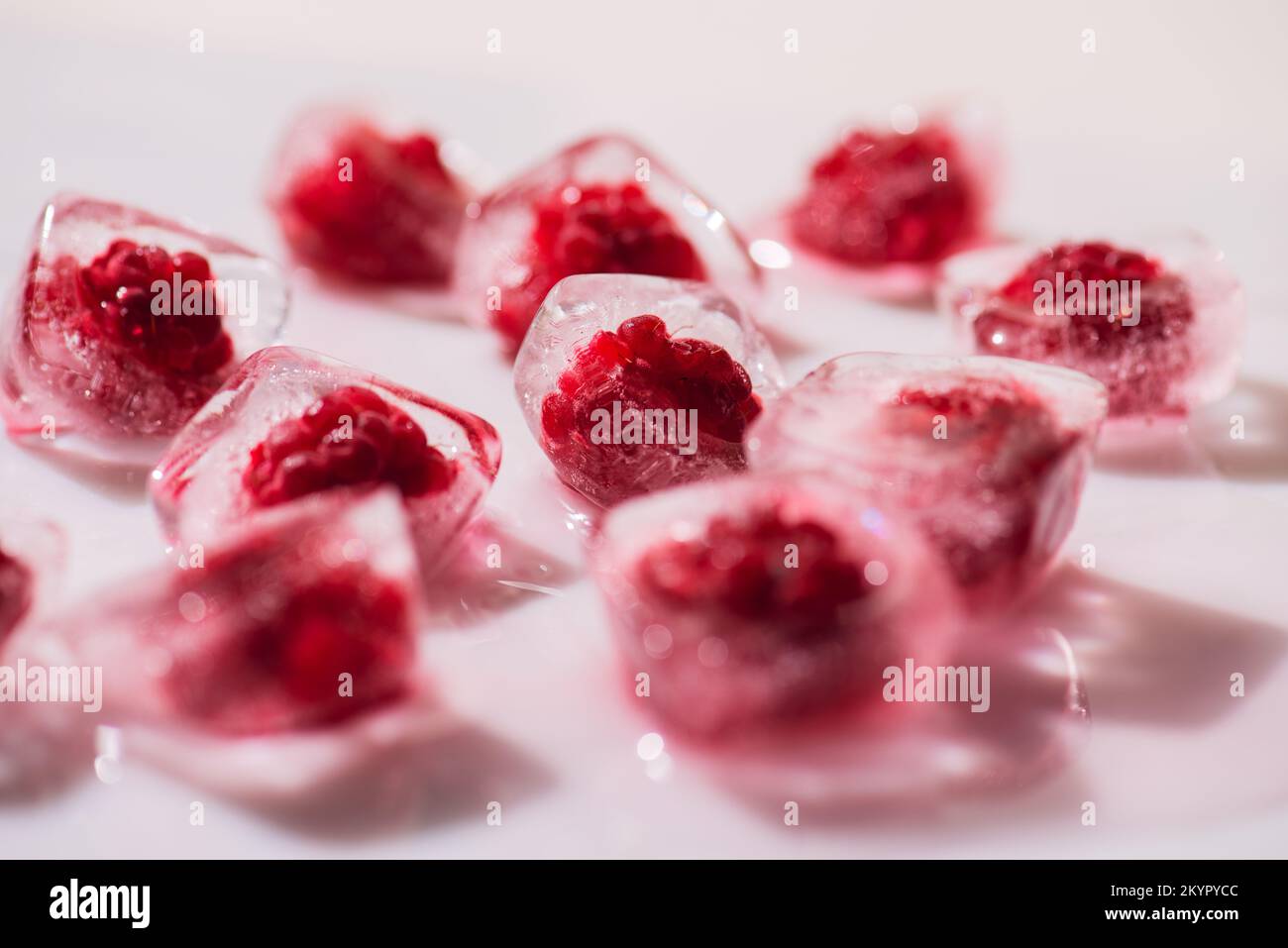 some frozen red raspberries inside ice cubes against white marble ...