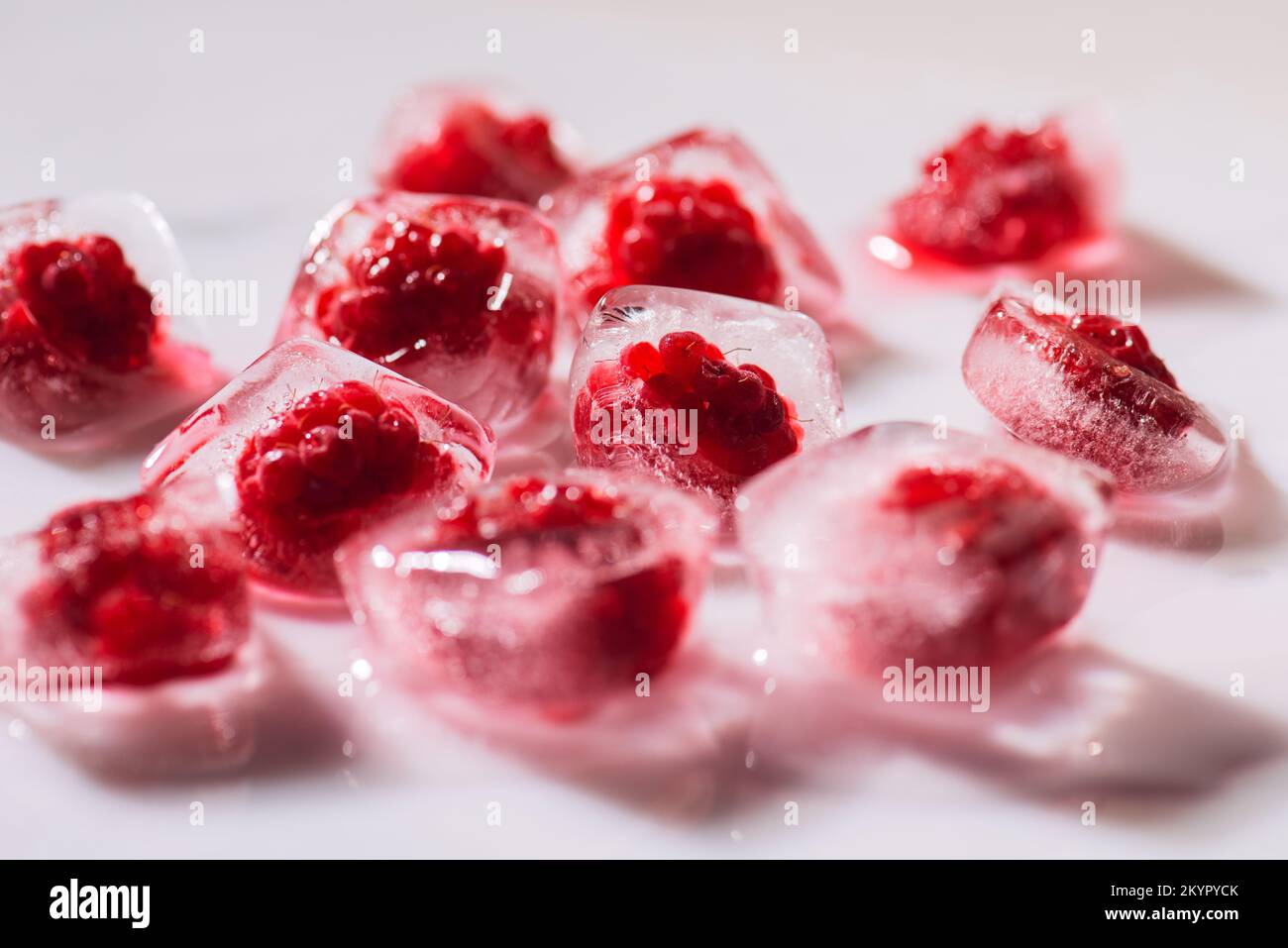 Frozen red raspberries inside ice cubes against white marble background ...
