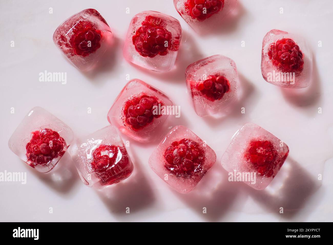 Frozen red raspberries inside ice cubes against white marble background ...