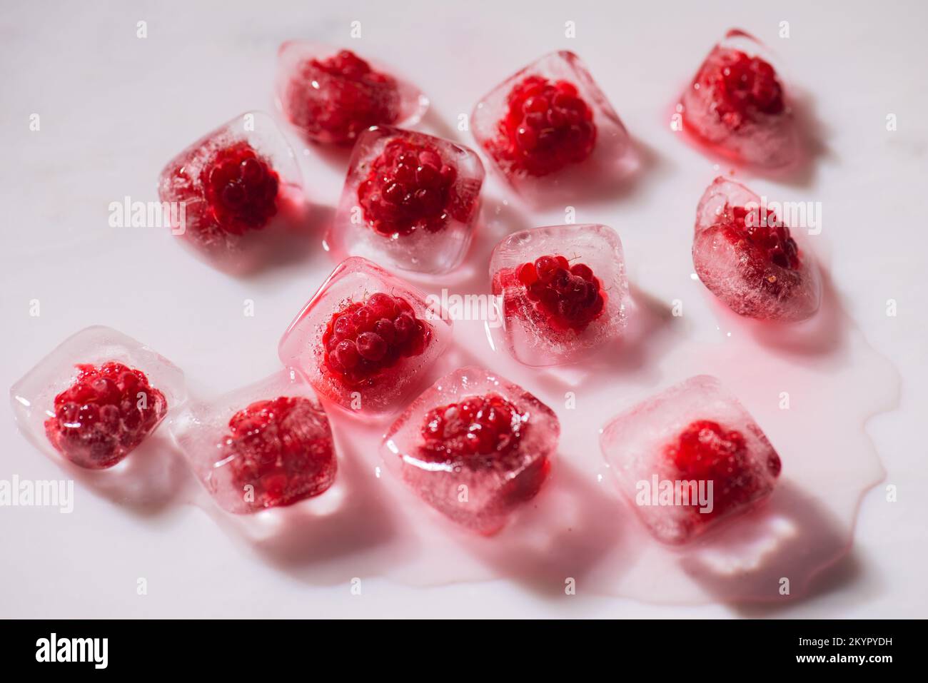 some frozen red raspberries inside ice cubes against white marble ...